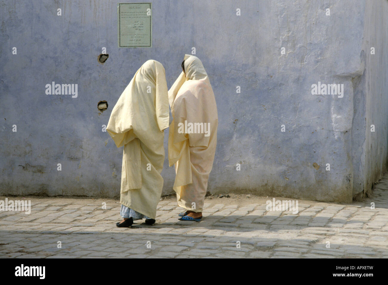 Women dressed in chadors on a paved sidewalk in Kairouan Stock Photo ...