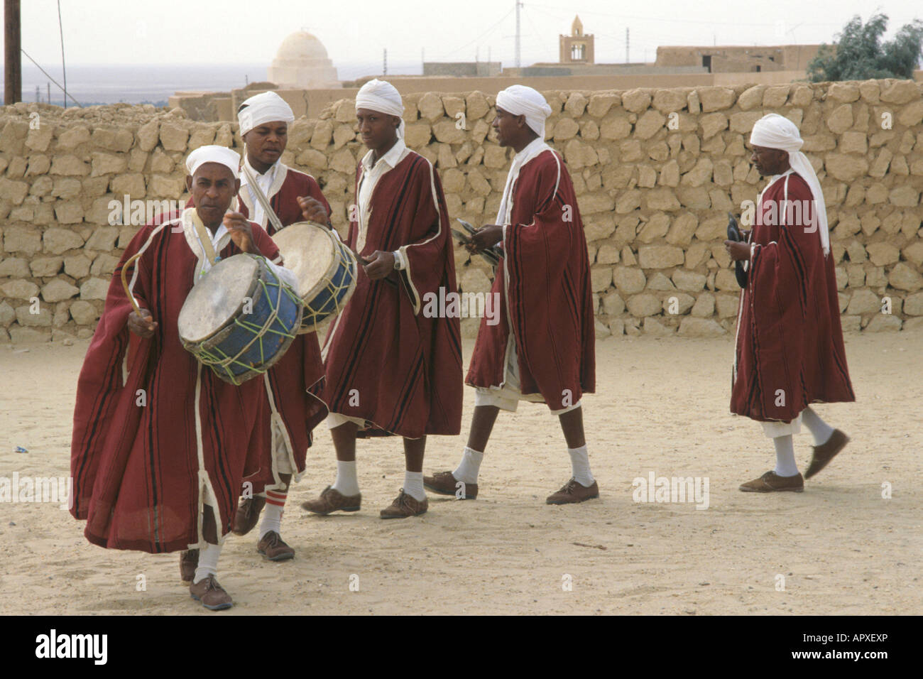 Tunisian musician in traditional robes walking in a line carrying ...