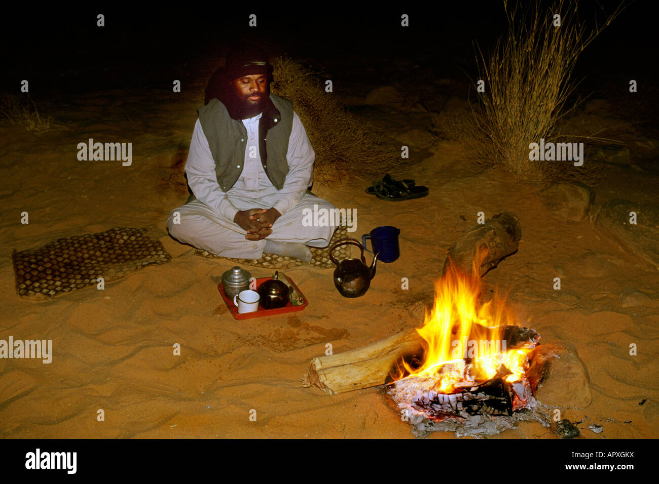Tuareg man sitting next a fire with small pots for making tea in front ...
