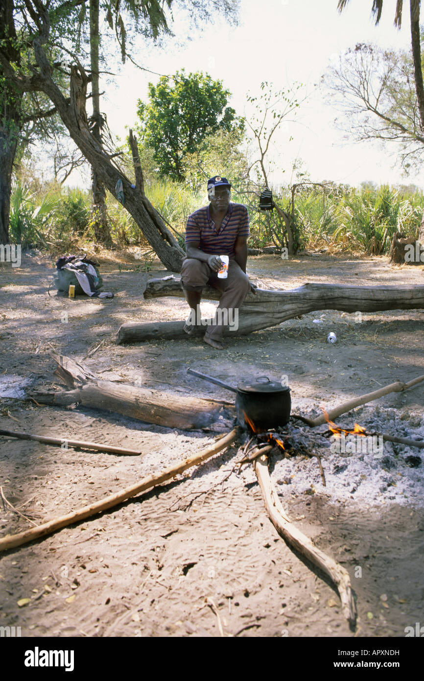Local man sitting on a tree stump with a traditional black cooking pot ...