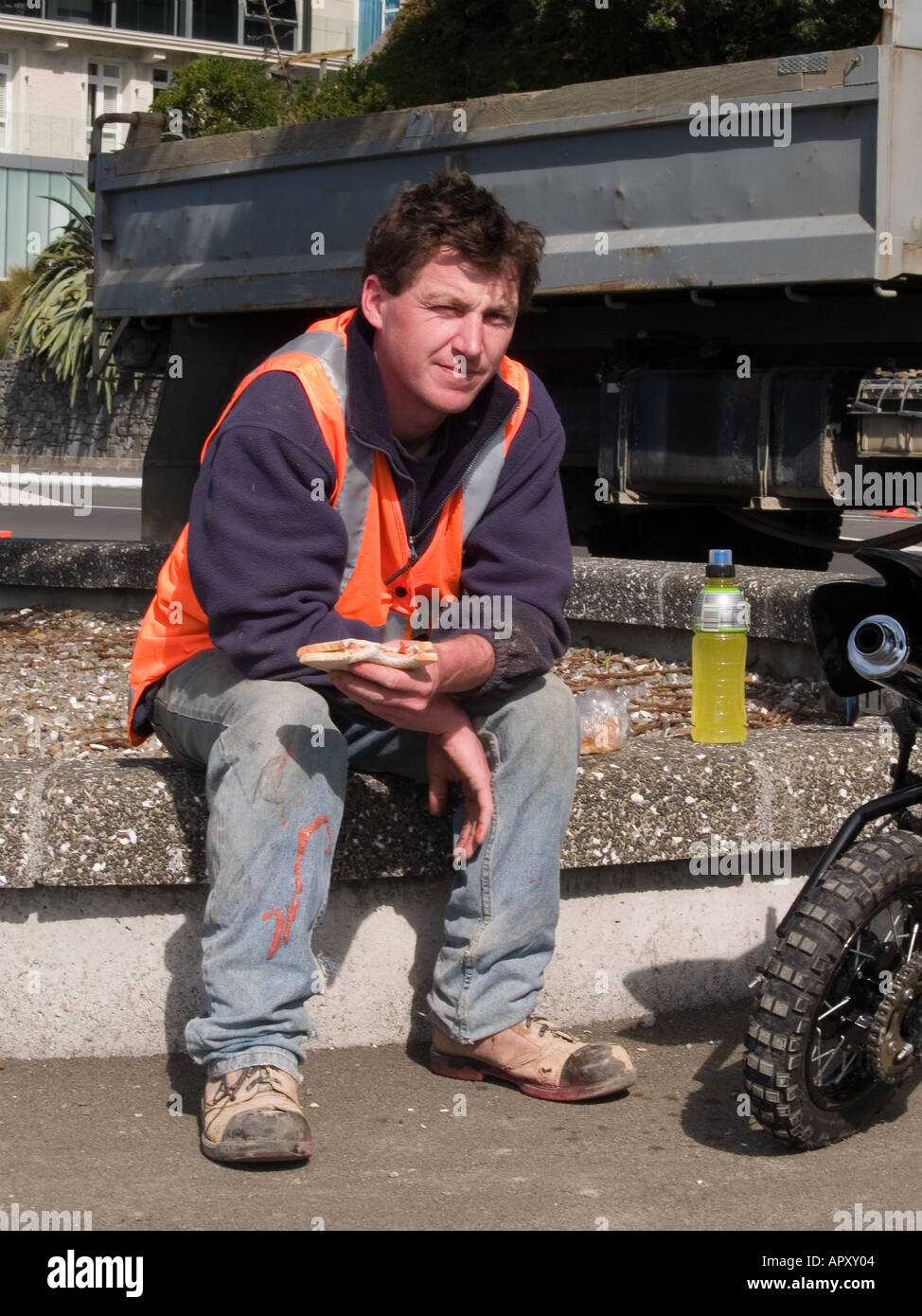 Workman wearing safety jacket eating his lunch with food and drink ...