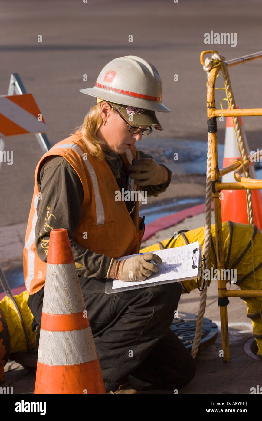 A female utility worker confers with her co-workers by walkie talkie as ...