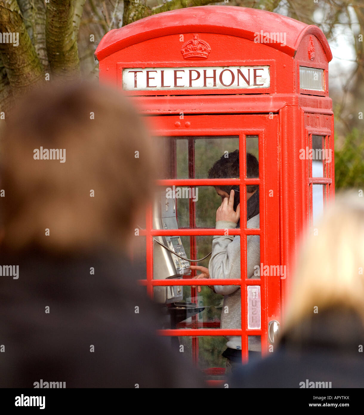 A young man using a red telephone box in a busy urban street. Picture ...