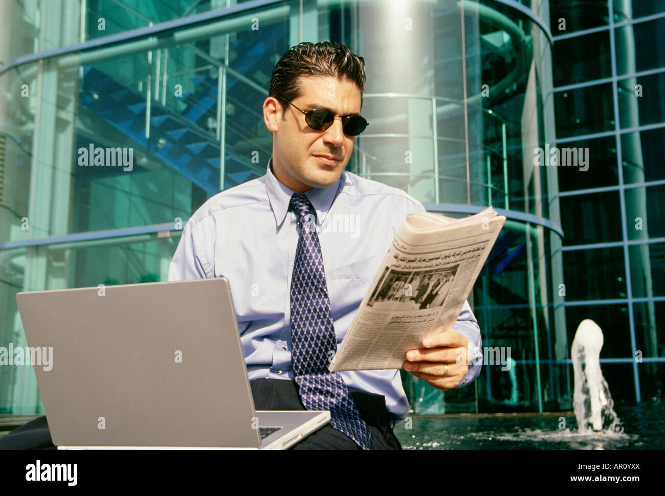 A man with laptop reading a newspaper with a commercial building at its ...