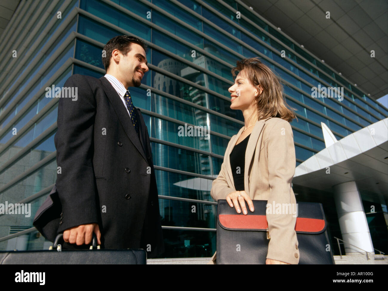 Businesspersons Talking outdoors in front of a modern glass building ...