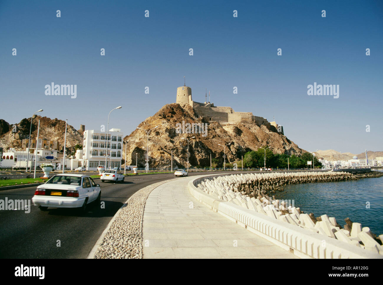 A fort is seen on the top of a cliff while cars cruise along the curved ...