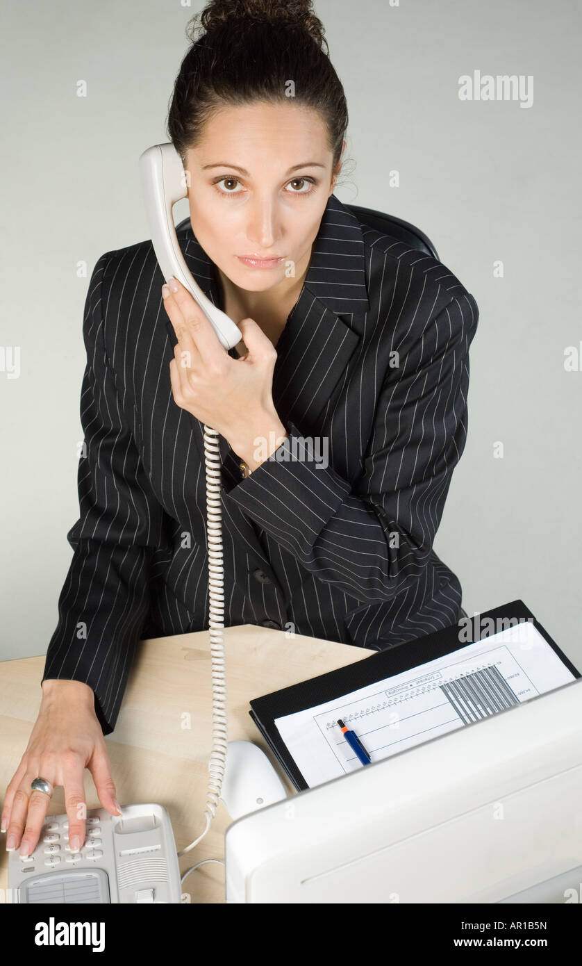 Woman sitting by desk, holding phone, portrait Stock Photo - Alamy