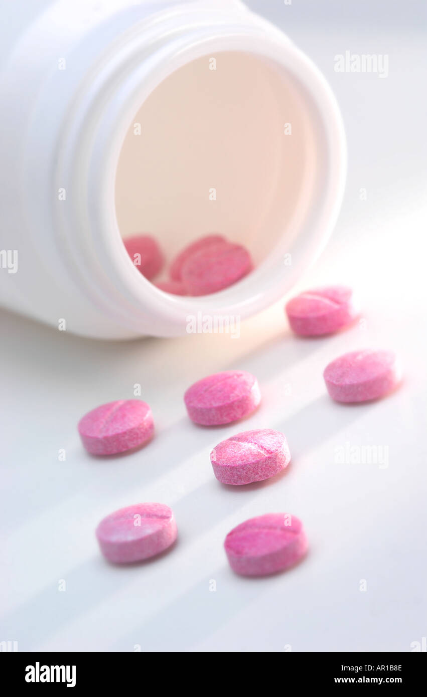 Pink tablets spilling out of white container Stock Photo - Alamy