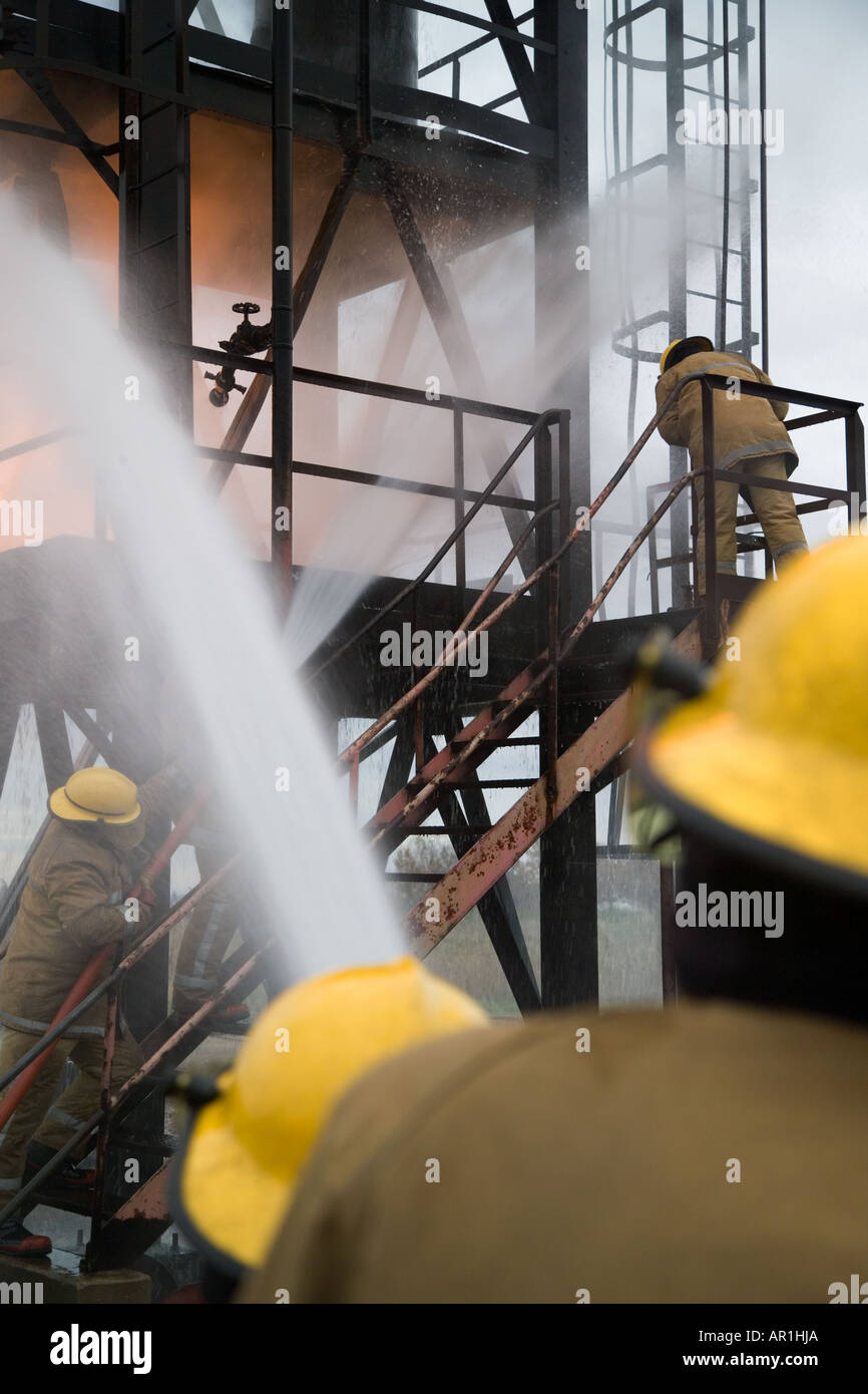 4 Firemen woring as a team together advancing fire behind water hose ...