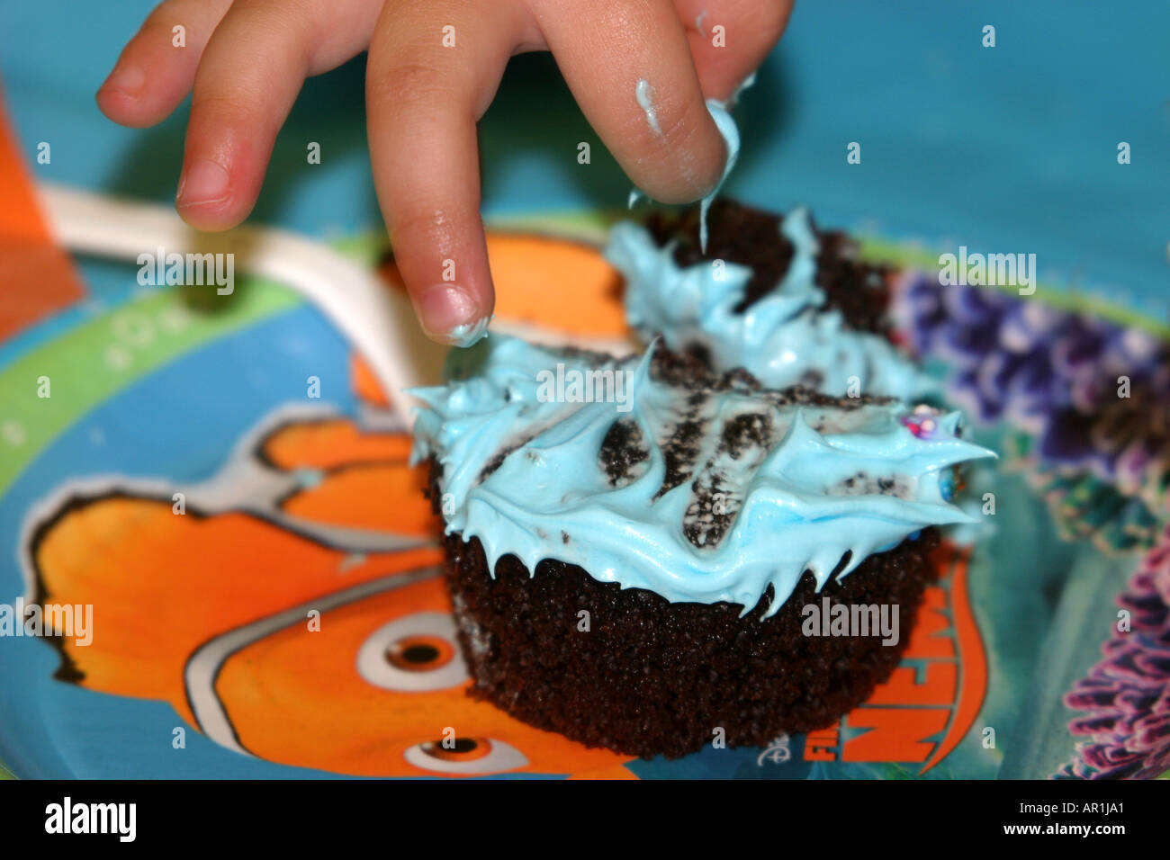Two year old child at a birthday party eating cake using his fingers to ...