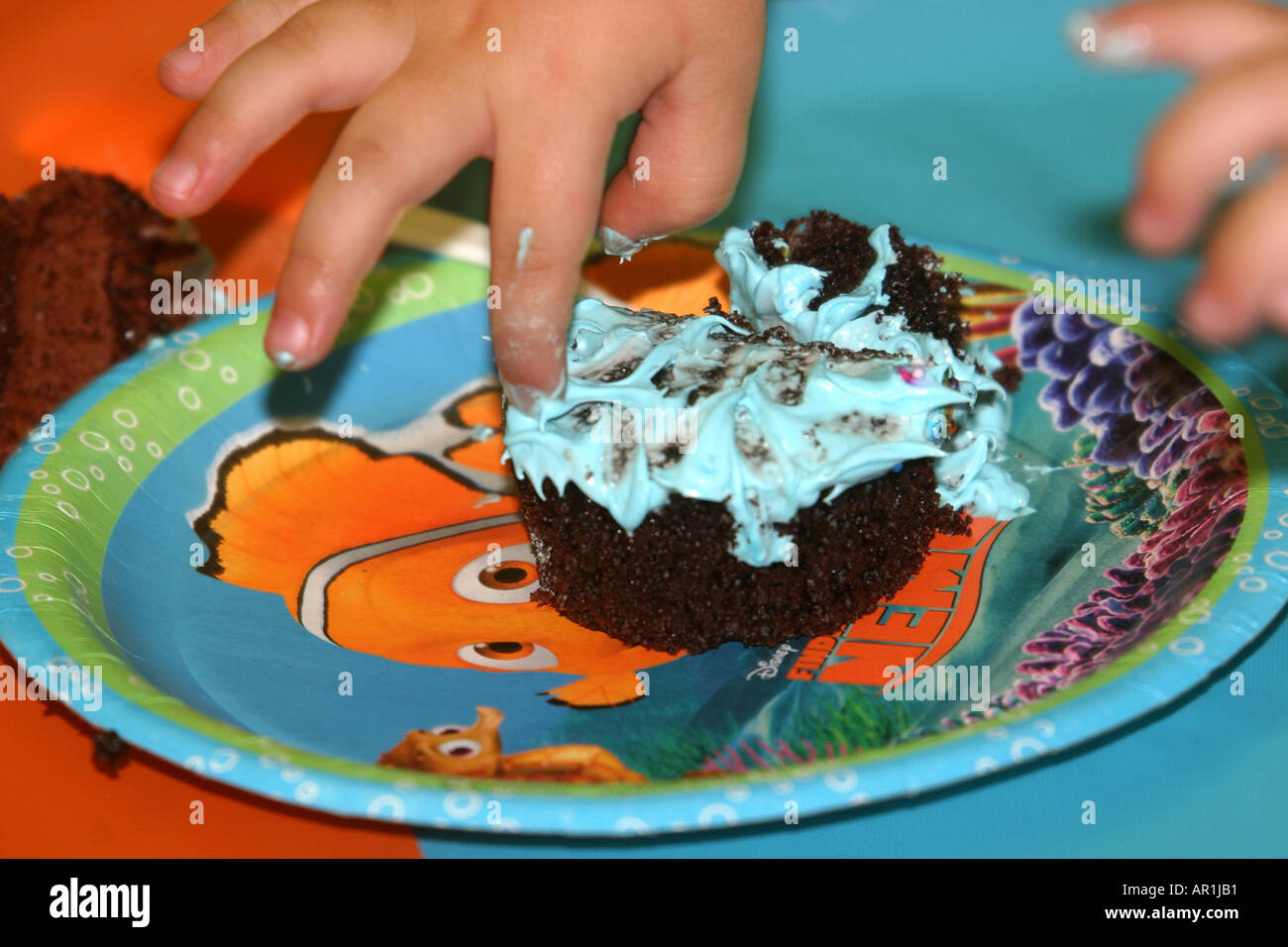 Two year old child at a birthday party eating cake using his fingers to ...