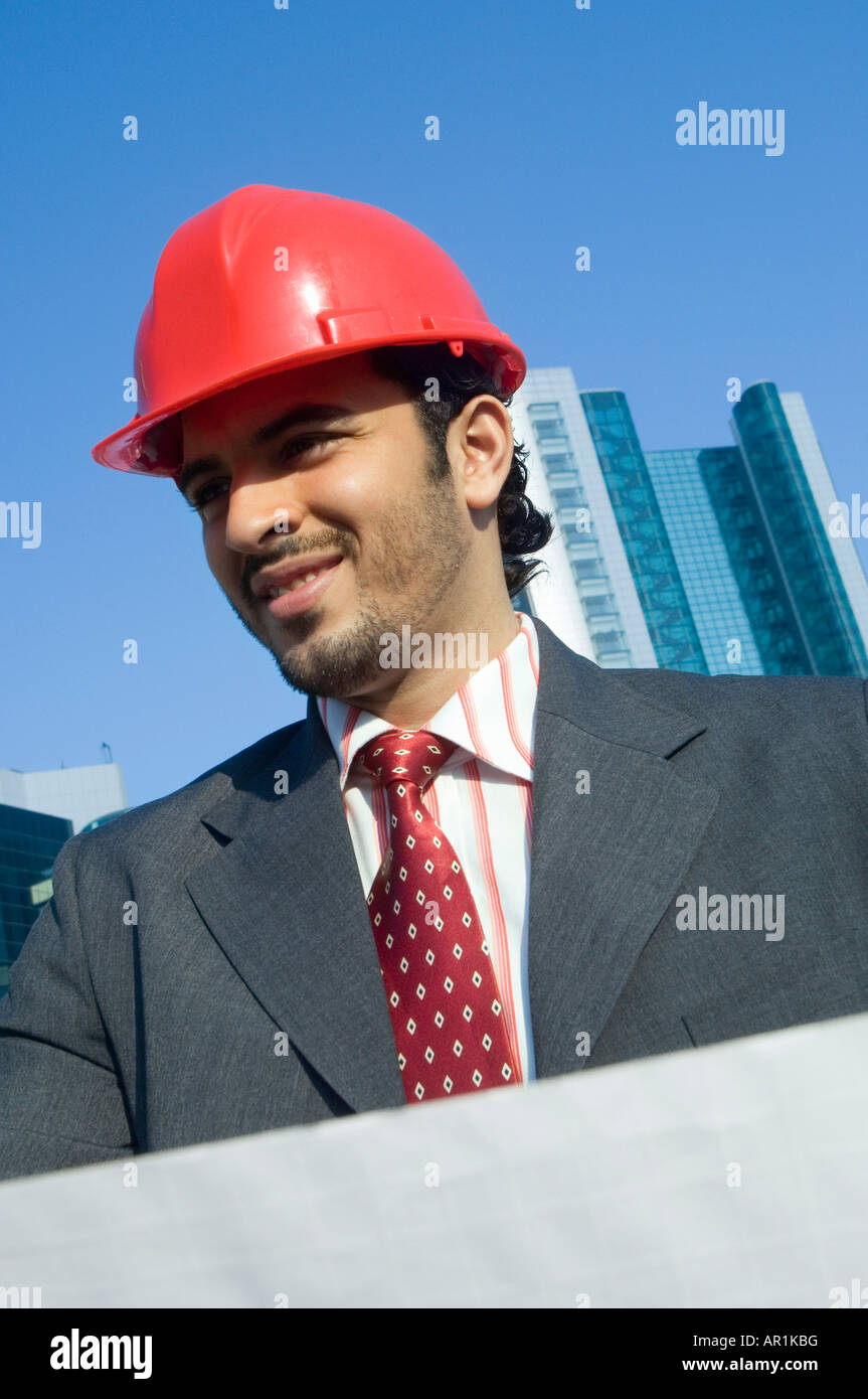Young man wearing a red hard hat outdoors with skyscrapers in the ...