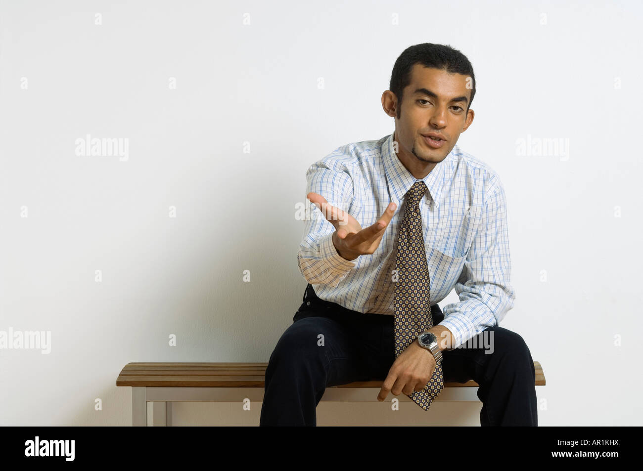 Young man sitting asking a question with hand gesture Stock Photo - Alamy