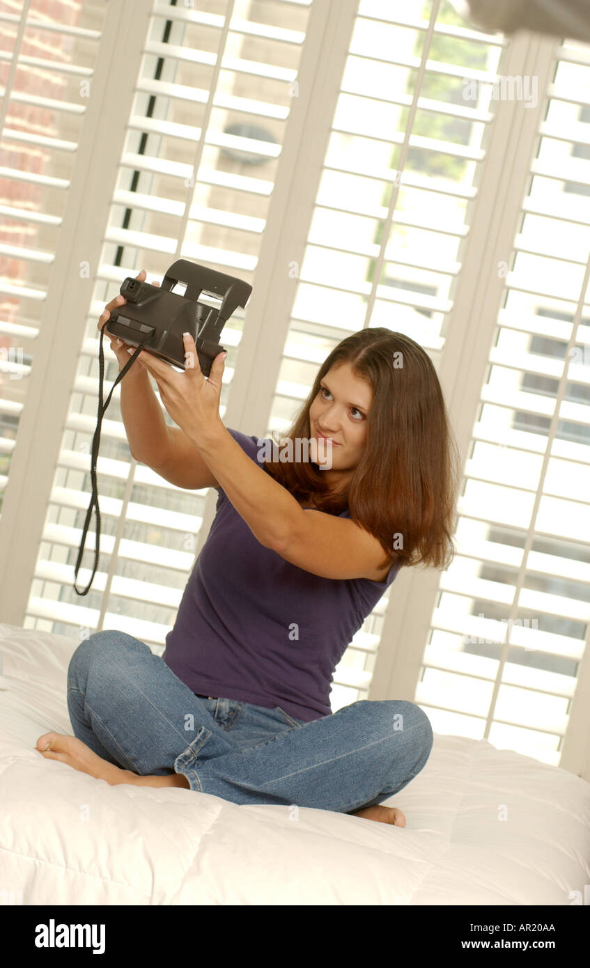 A female on a bed holding a video camera up above her head filming ...