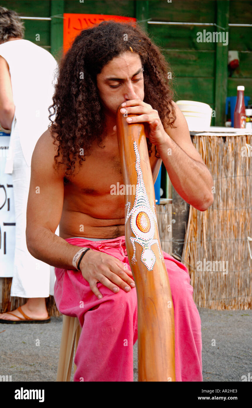 a young man in his 20s blowing into a didjeridu, an Aboriginal music ...