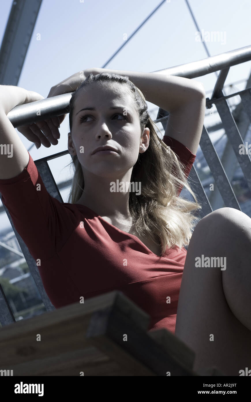 young woman in red sitting on a bench with her arms over a railing ...