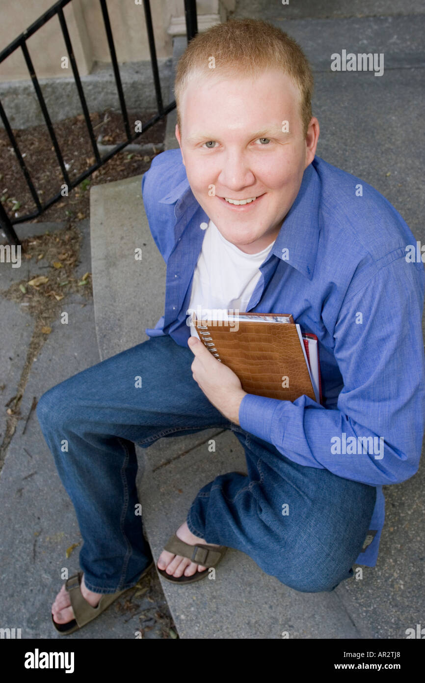 Man sitting on steps holding books under his arm smiling Stock Photo ...