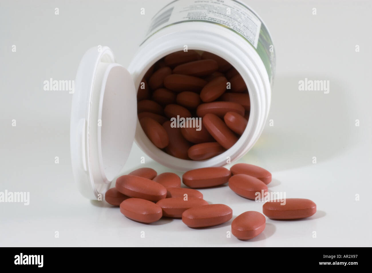 Red tablets spilling from a white container Stock Photo - Alamy