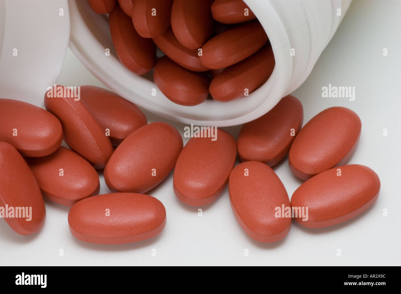 Red tablets spilling from a white container Stock Photo - Alamy