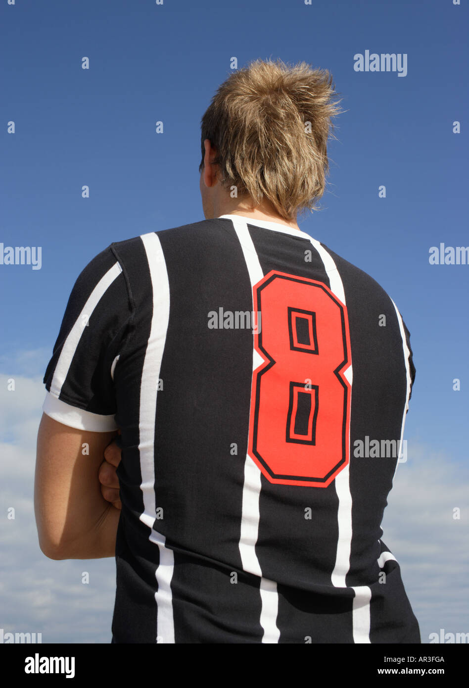 Young man wearing a number 8 football shirt standing against blue sky ...