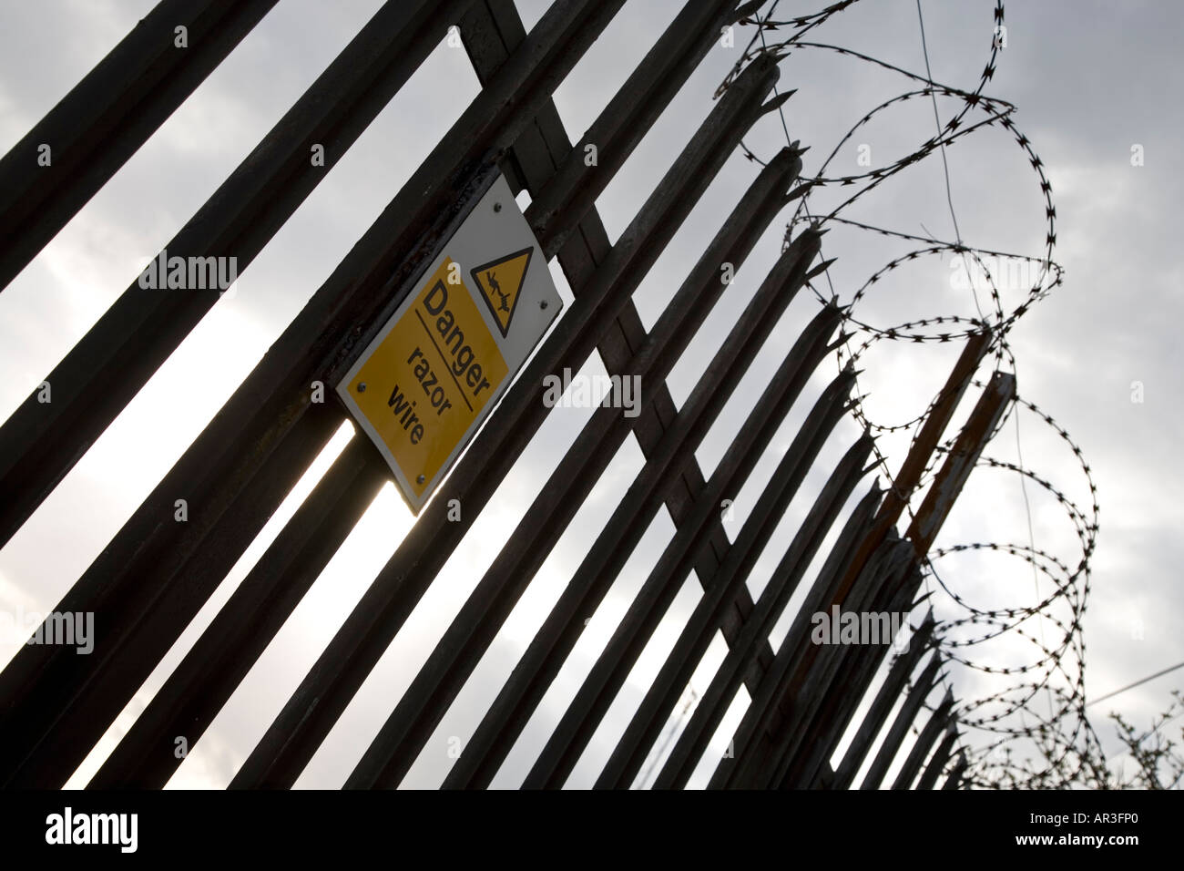 A tall metal fence with barbed wire on the top, a warning sign reading ...