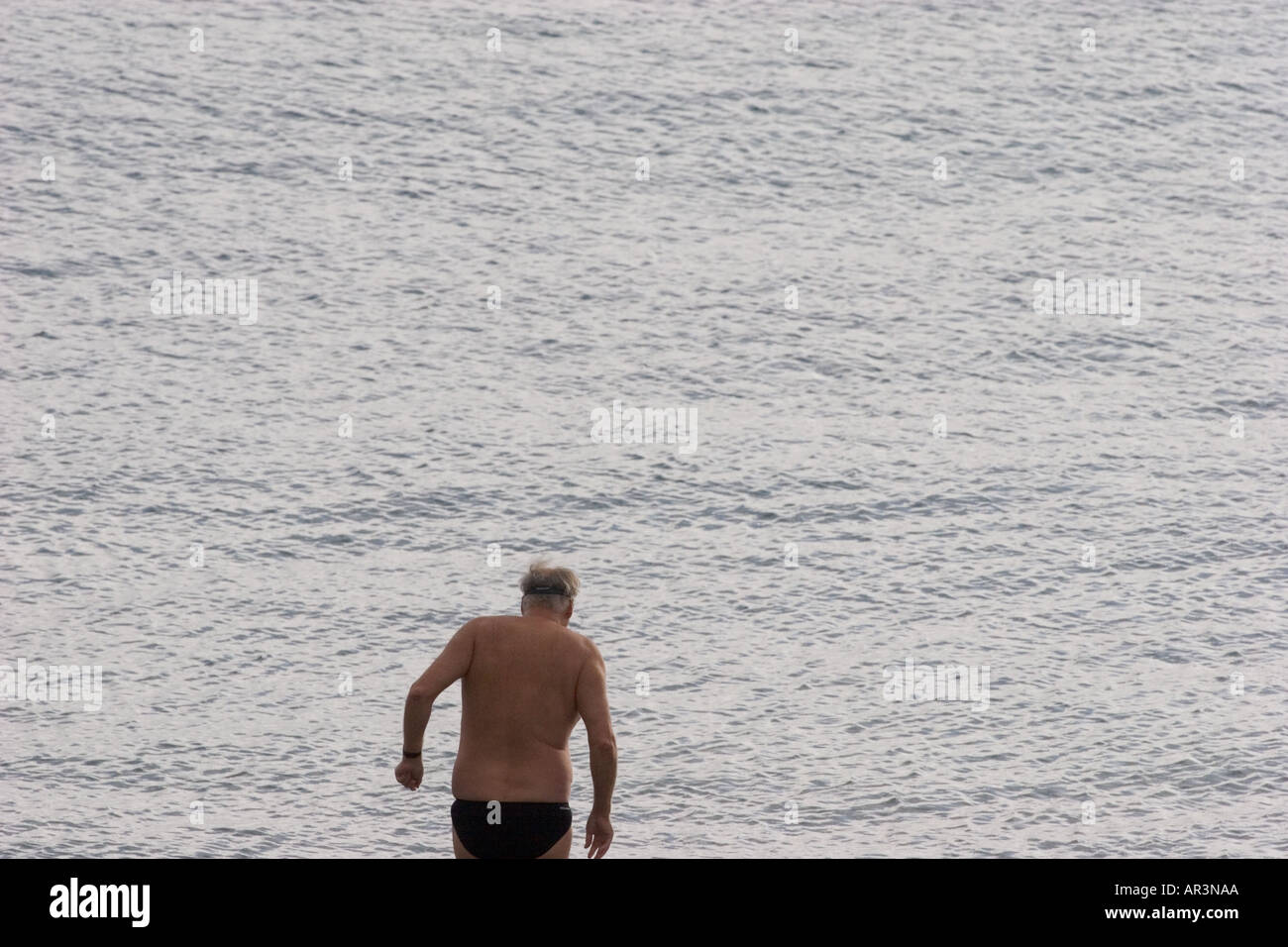 Elderley swimmer entering sea for early morning swim, Jersey, Channel ...