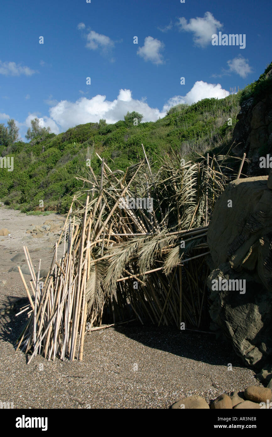 A home made cabana sun shelter of palm leaves on rocky coastline west ...