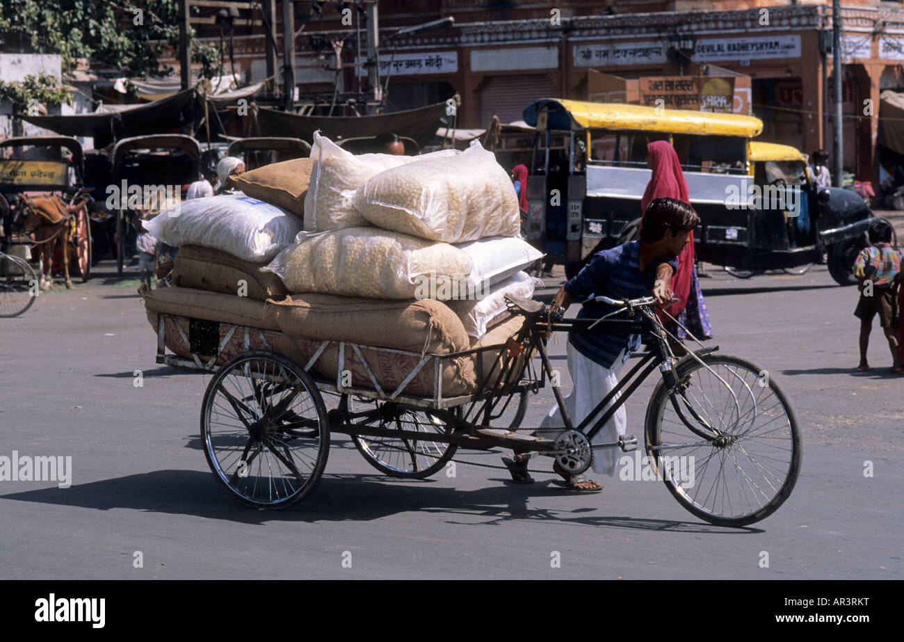 A worker pushing a heavy loaded rickshaw through a busy street, Jaipur ...
