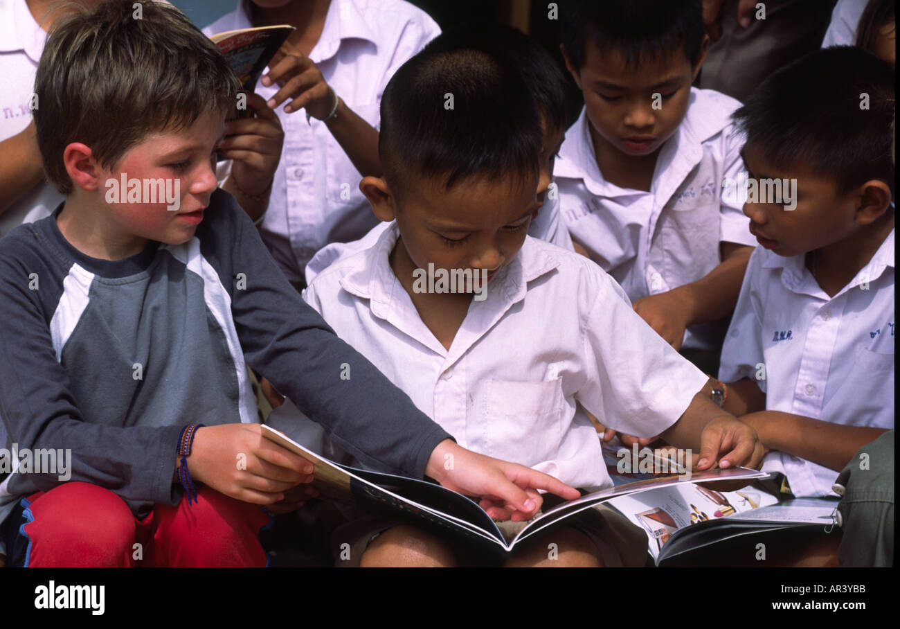 British boy showing local Thai schoolboy an English book, as he visits ...