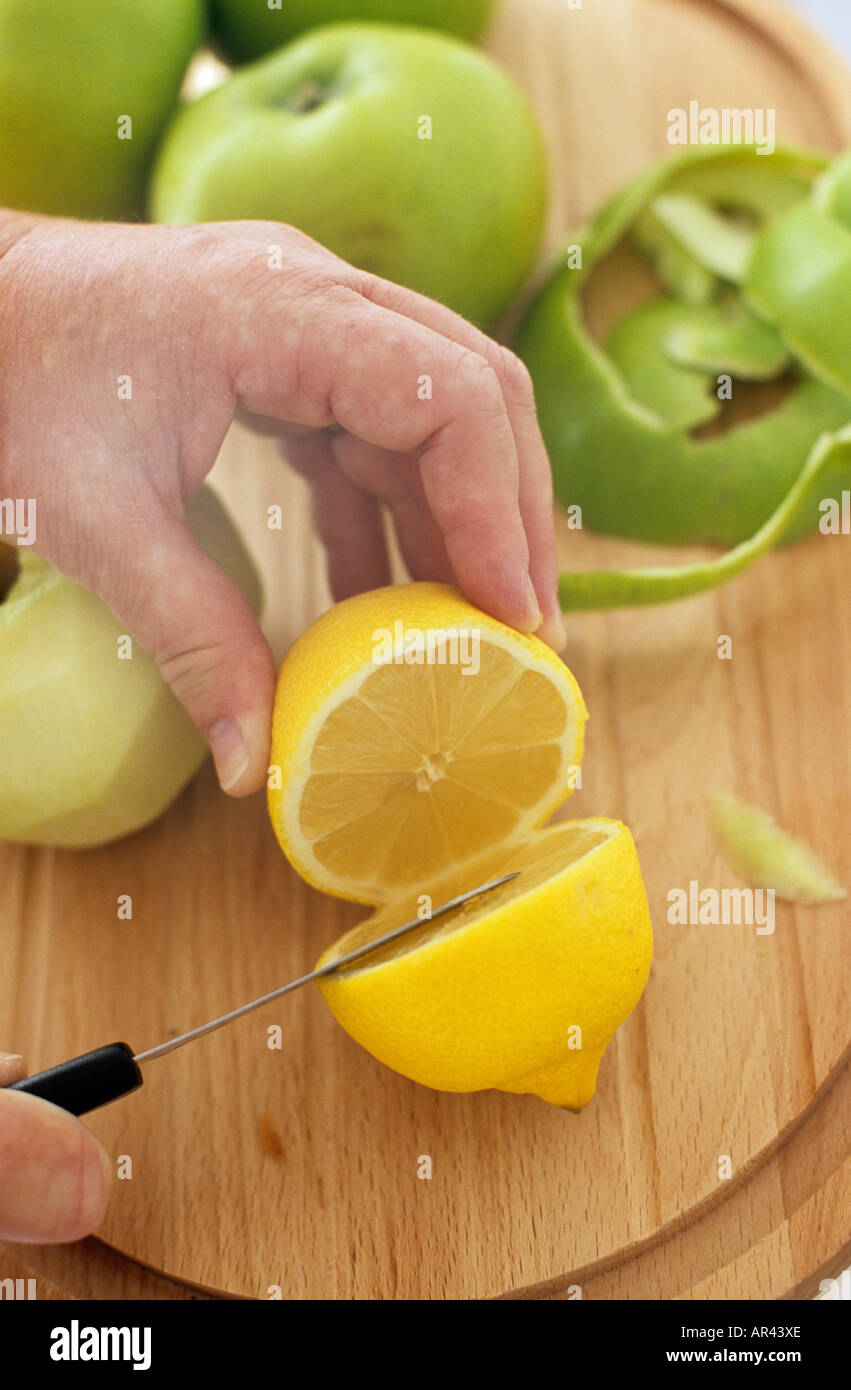LEMON BEING CUT WITH KNIFE ON WOODEN CHOPPING BOARD WITH UNPEELED AND ...