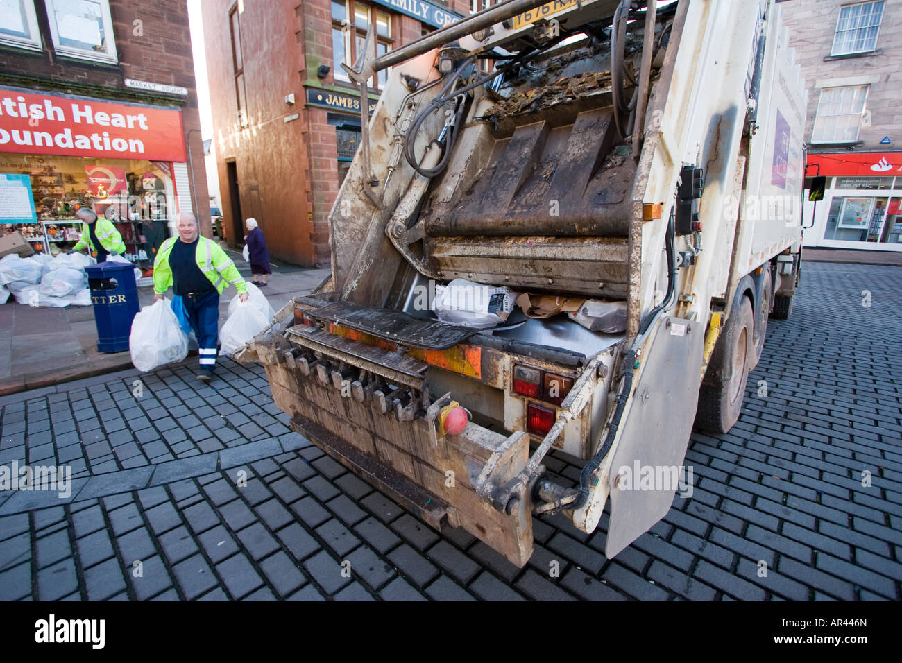 A garbage collection worker prepares to toss bags of litter in the back ...