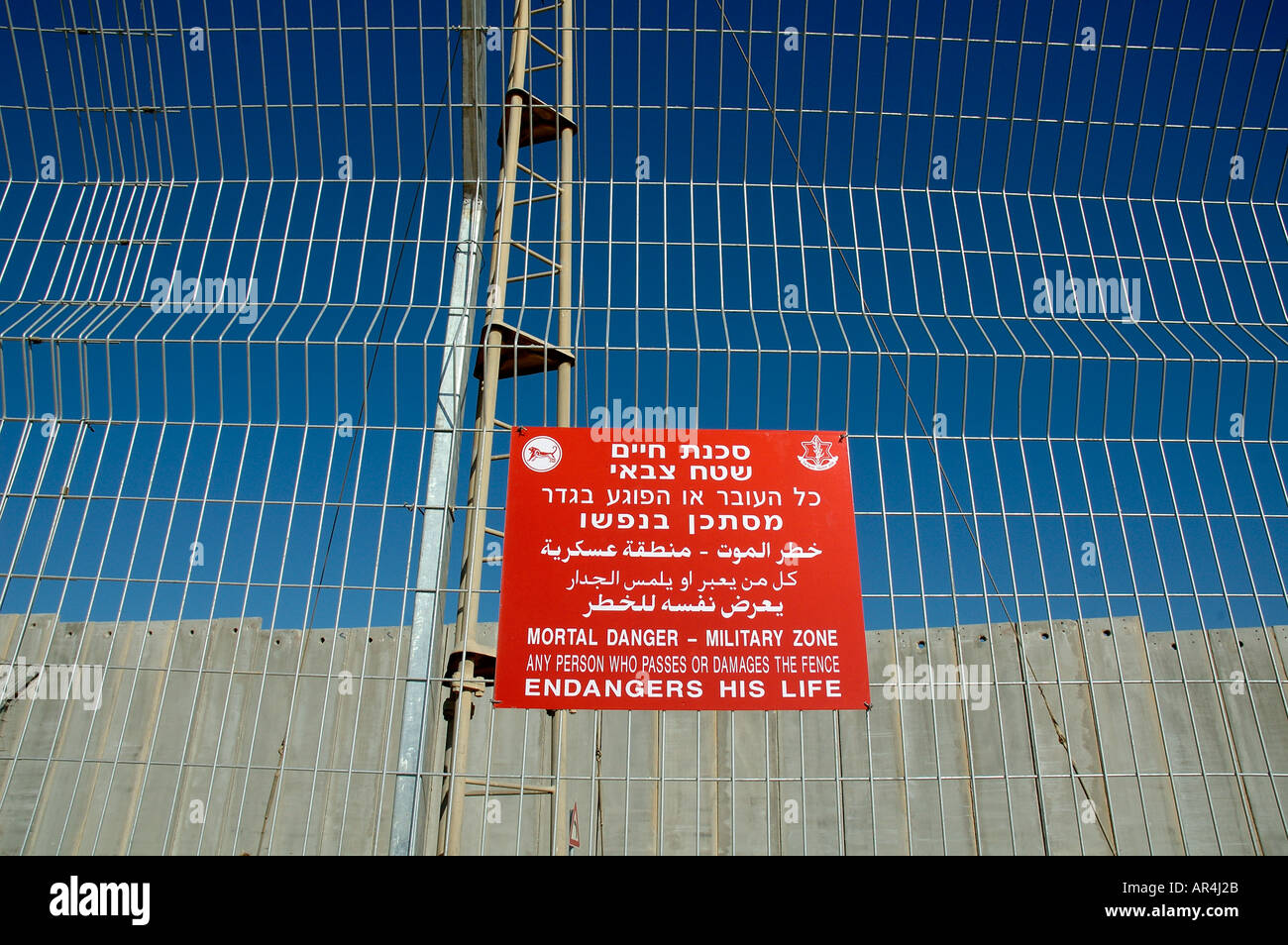 Warning sign hanged on wire fence with concrete defense wall ...