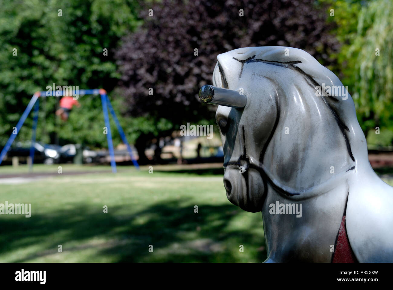 Playground equipment, a white horse, with child on swing out of focus ...