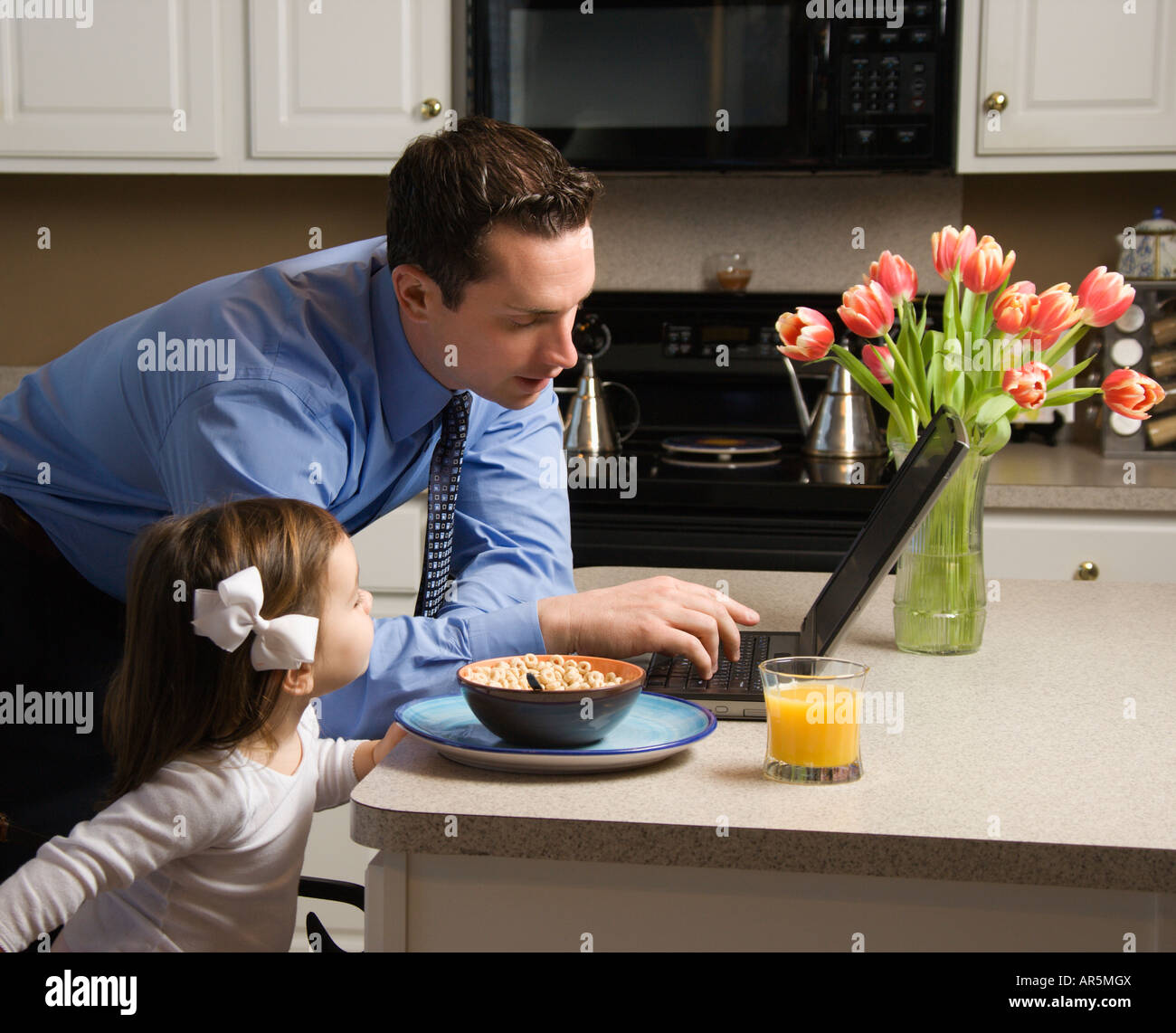 Caucasian father in suit using laptop computer with daughter eating ...
