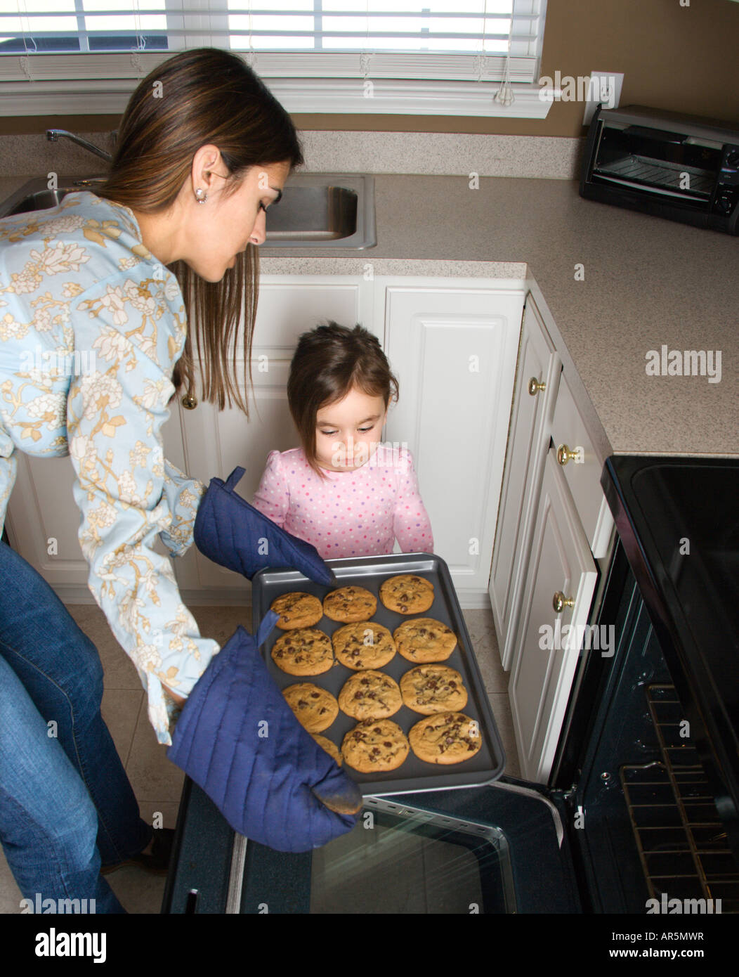 Caucasian mother and daughter taking cookies out of oven Stock Photo ...