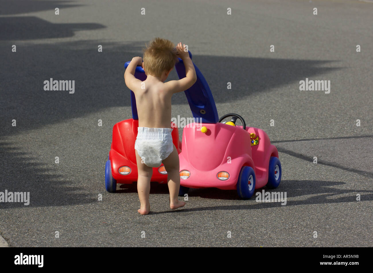 toddler pushing two toy cars on street Stock Photo - Alamy