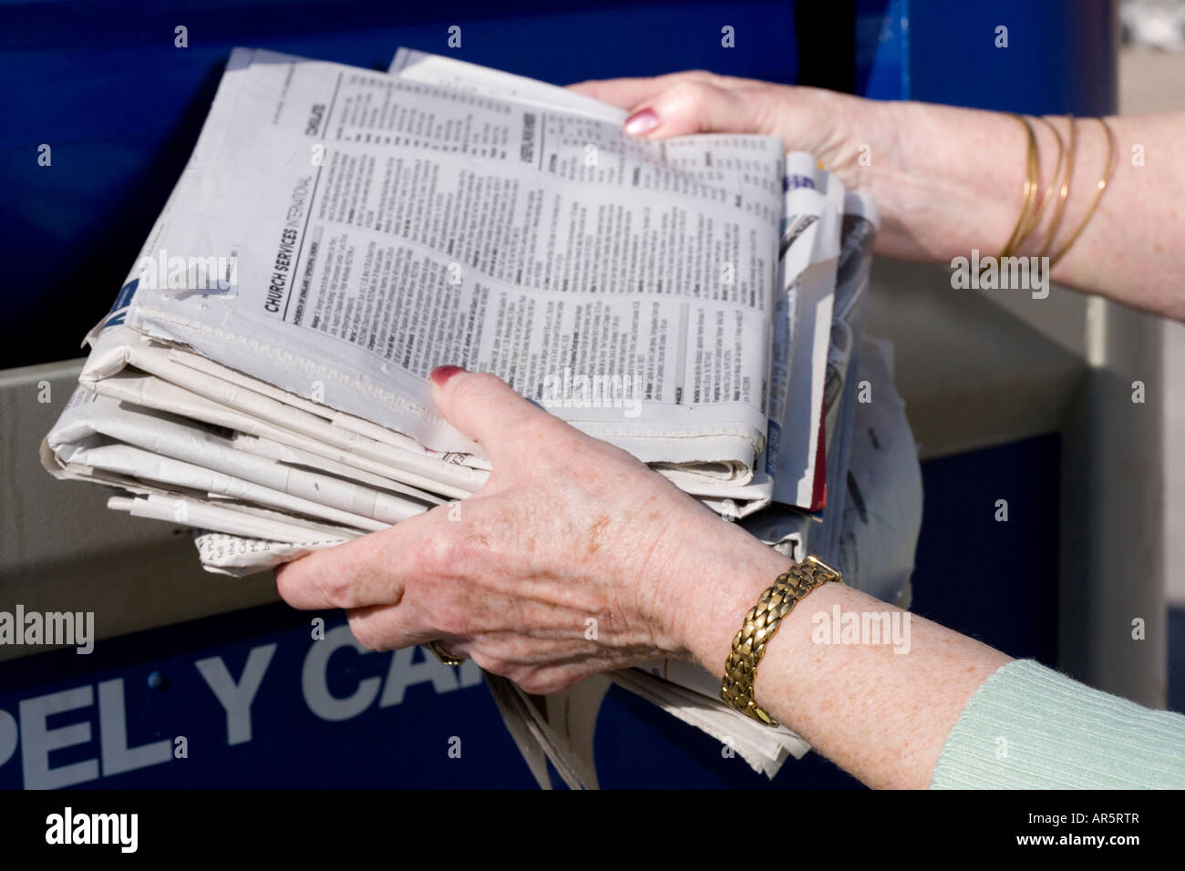 Close up of senior woman's arms throwing newspaper into recycle bin ...