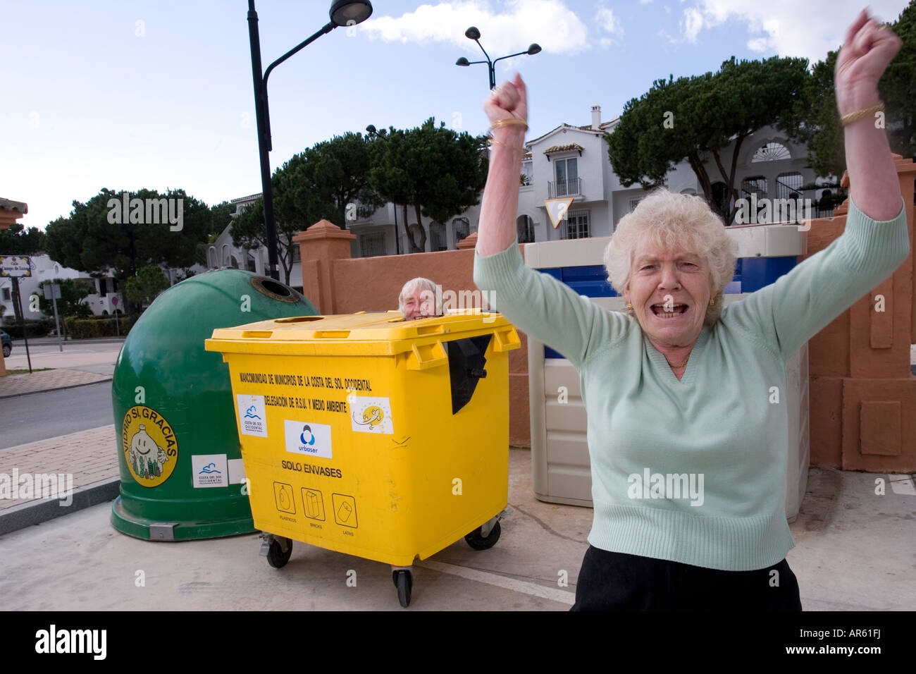Senior woman clenching fist with man in recycle bin in background Stock ...