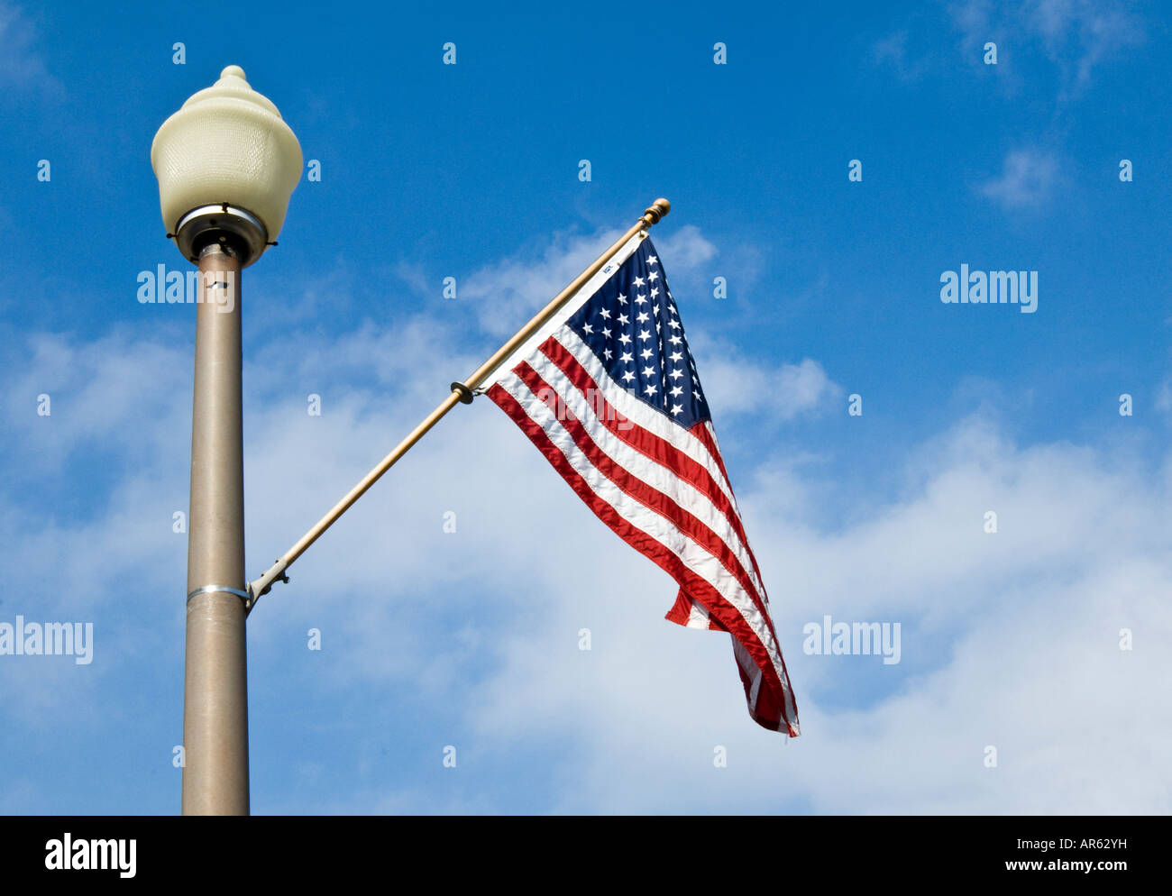 American Flag attached to lamp post waves against blue sky with fluffy ...