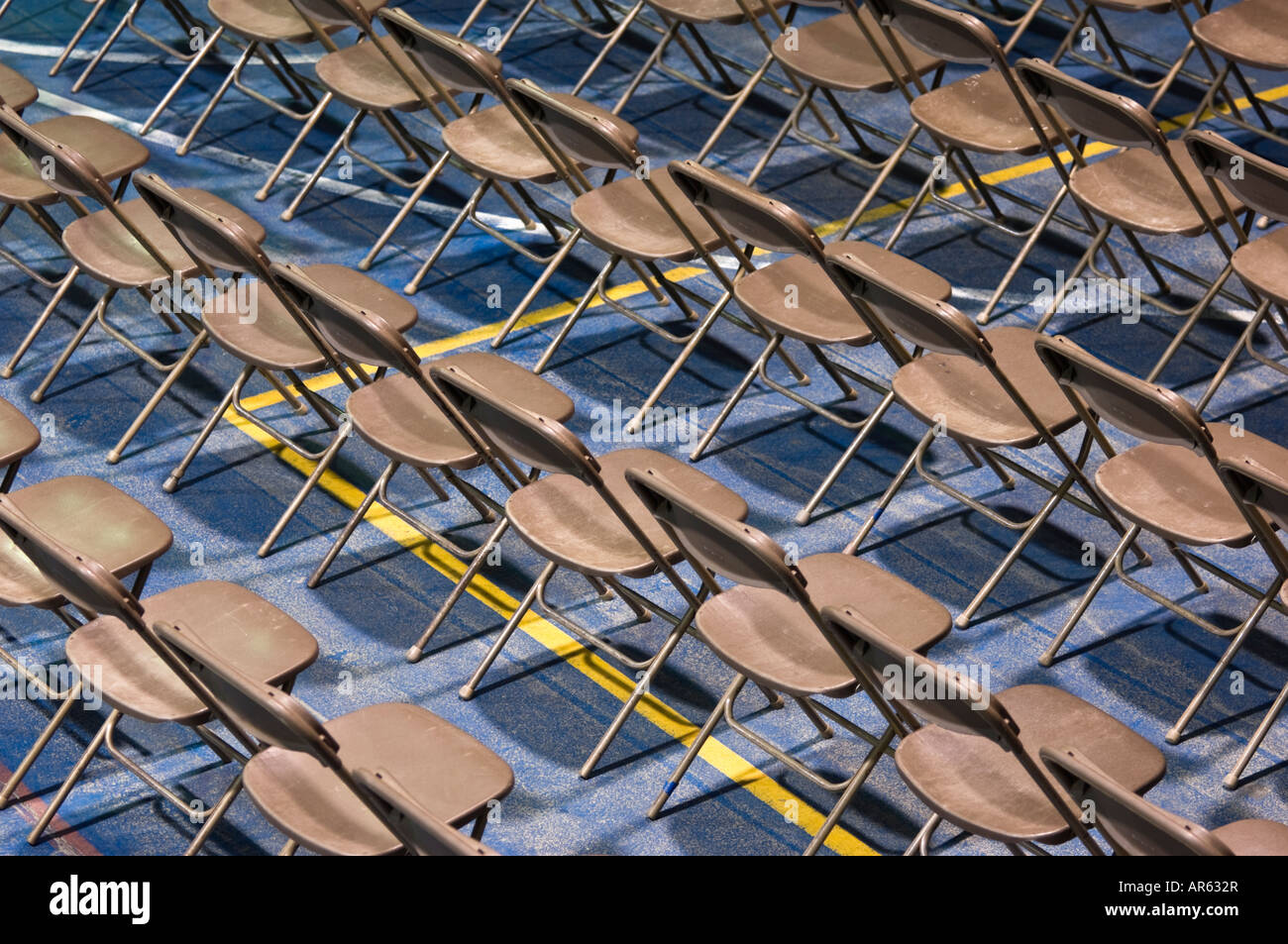 Diagonal rows of empty folding chairs set up on a very worn gym floor ...
