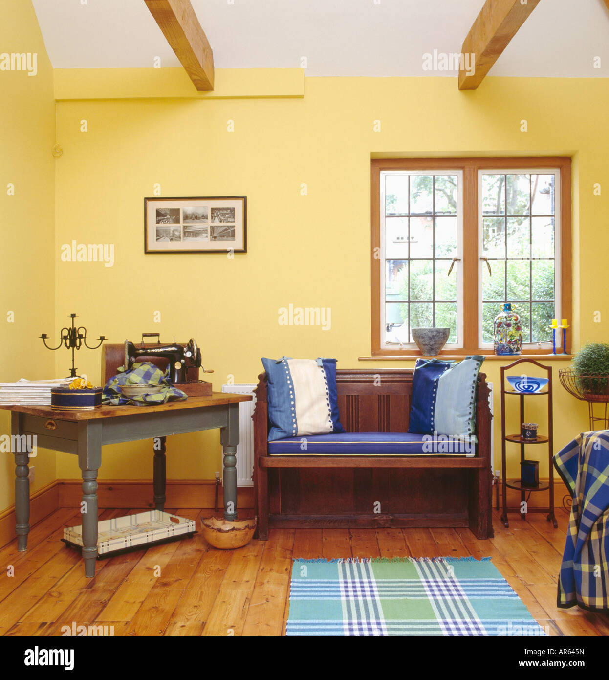 Sewing machine on table beside wooden settle with blue cushions below ...
