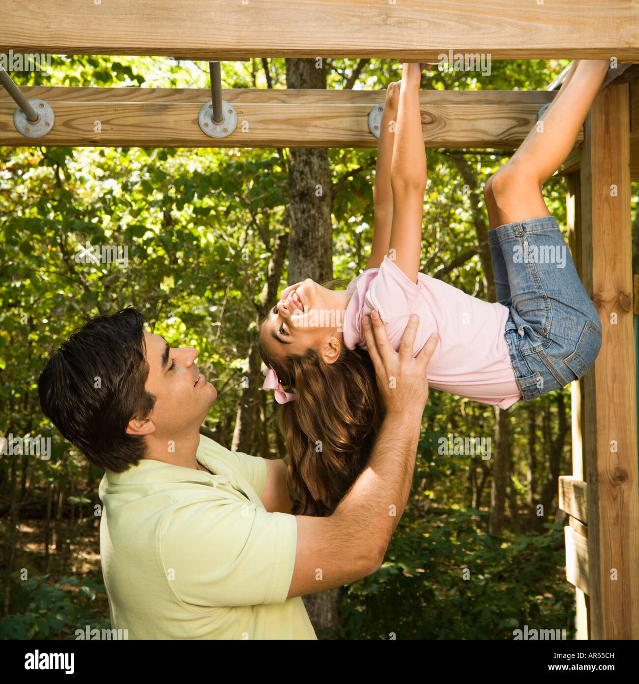 Hispanic girl hanging by arms and legs from monkey bars smiling at ...