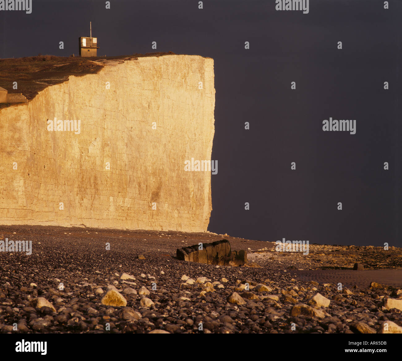 Face of Birling Gap cliff lit by the sun very dark sky and shingle ...