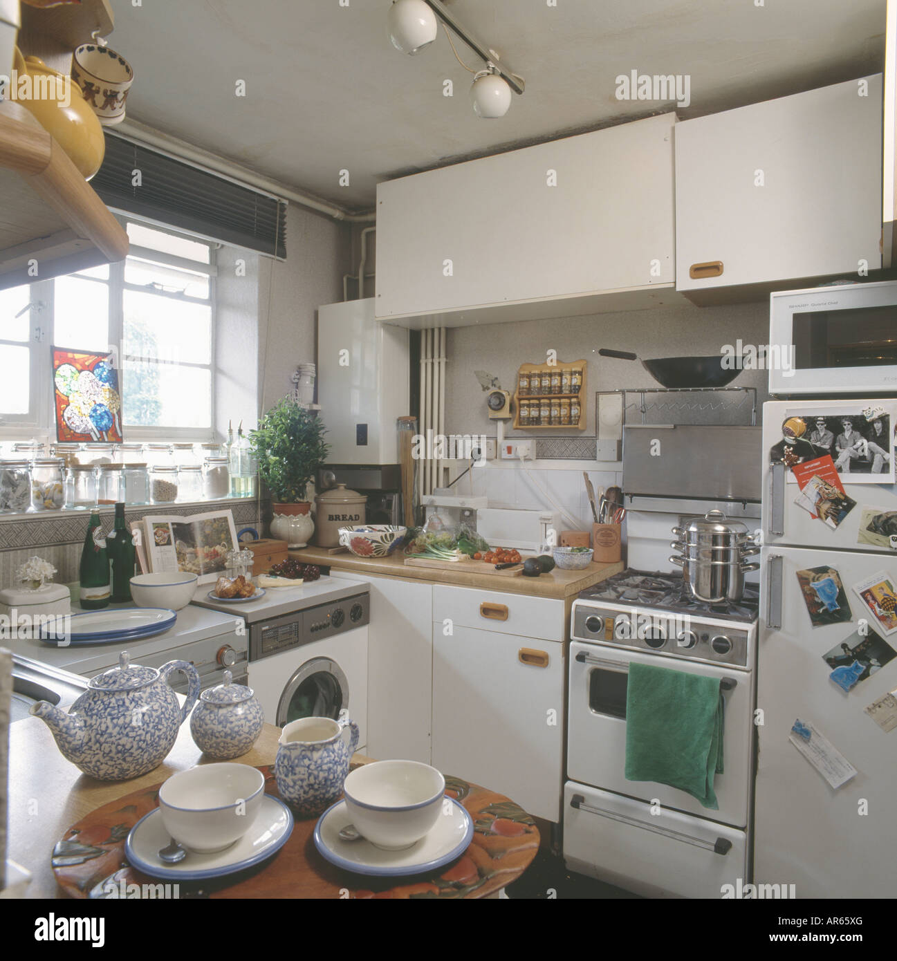 Teapot and cups on worktop in compact white kitchen with oven and ...