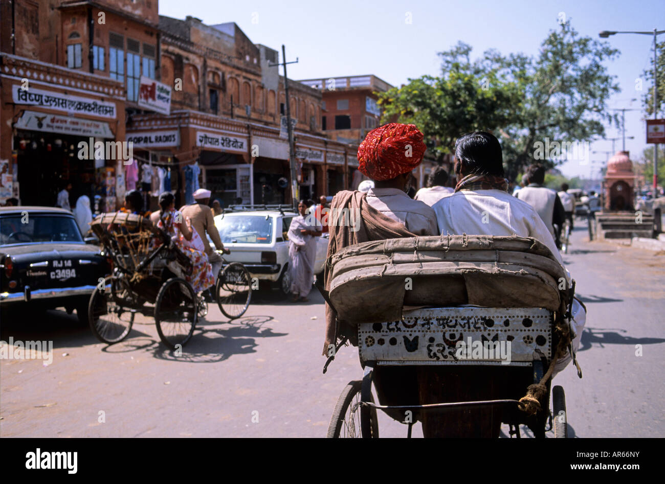 A Sikh wearing a red turban taking a rickshaw taxi ride in a busy ...