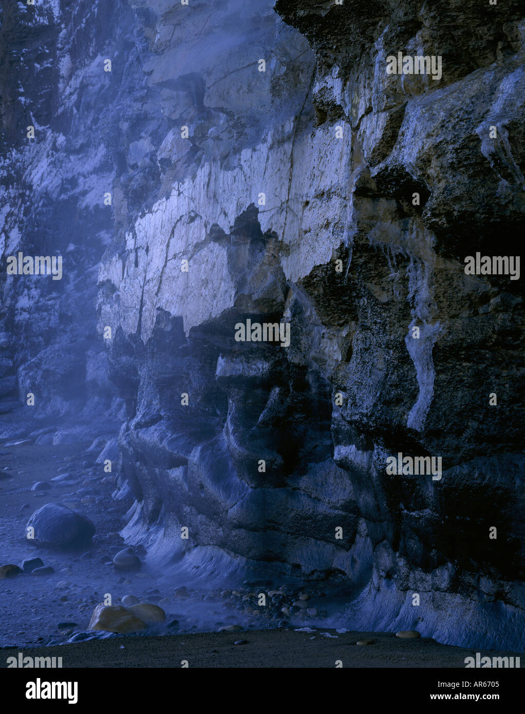 A half frozen waterfall on the crumbling cliff face and on the rocky ...