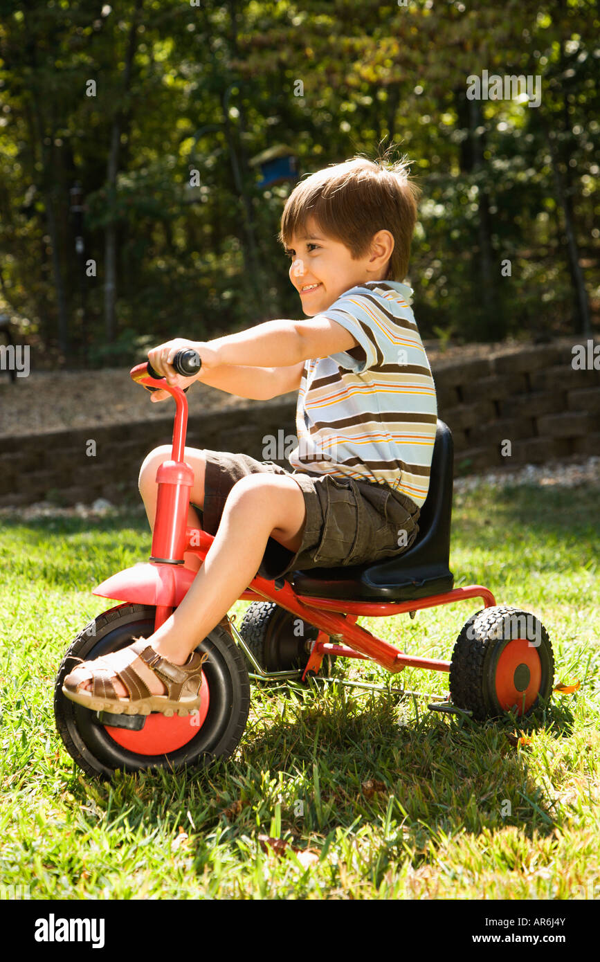 Side view of Hispanic boy riding red tricycle in grass Stock Photo - Alamy