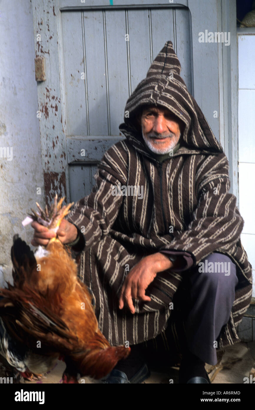 Old Muslim Man with hood in scary expression with chicken in hand in ...