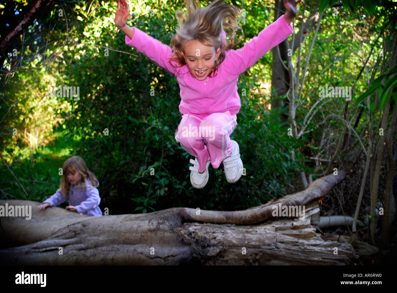 8 year old female child jumping off fallen log, little sister in ...