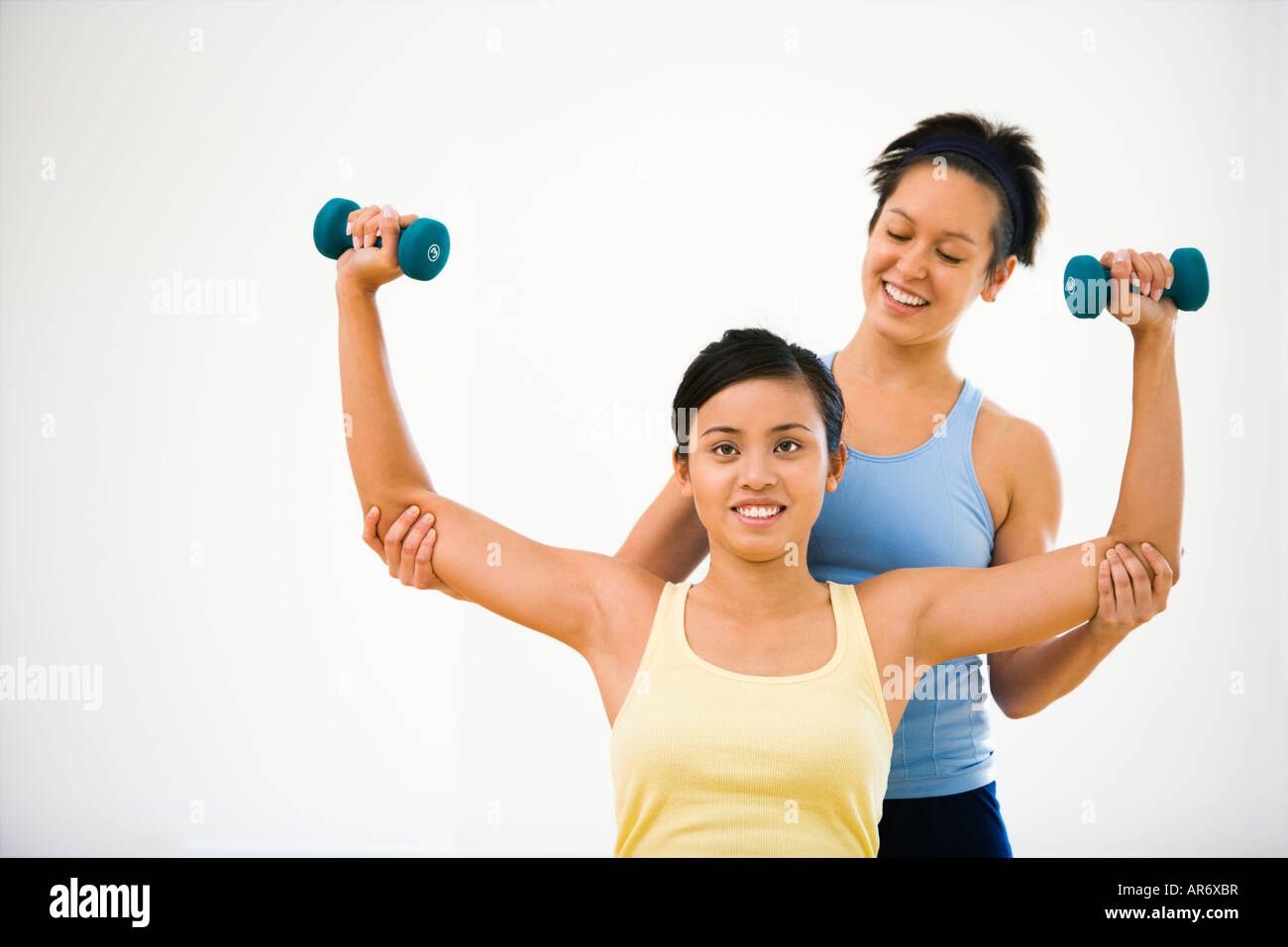 Young woman lifting hand weights while another woman helps position her ...